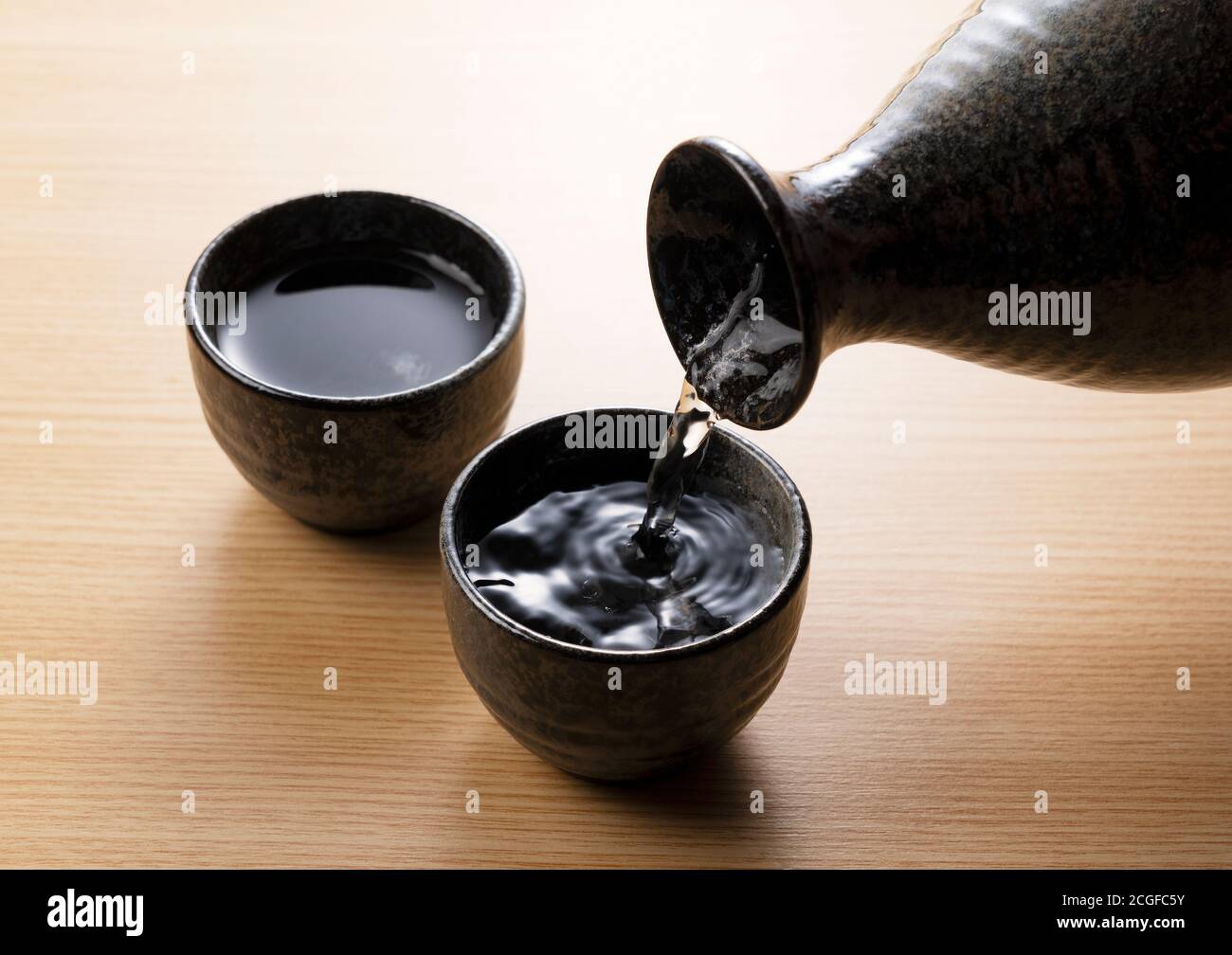 Pouring sake into a sake cup set against a wooden backdrop Stock Photo ...