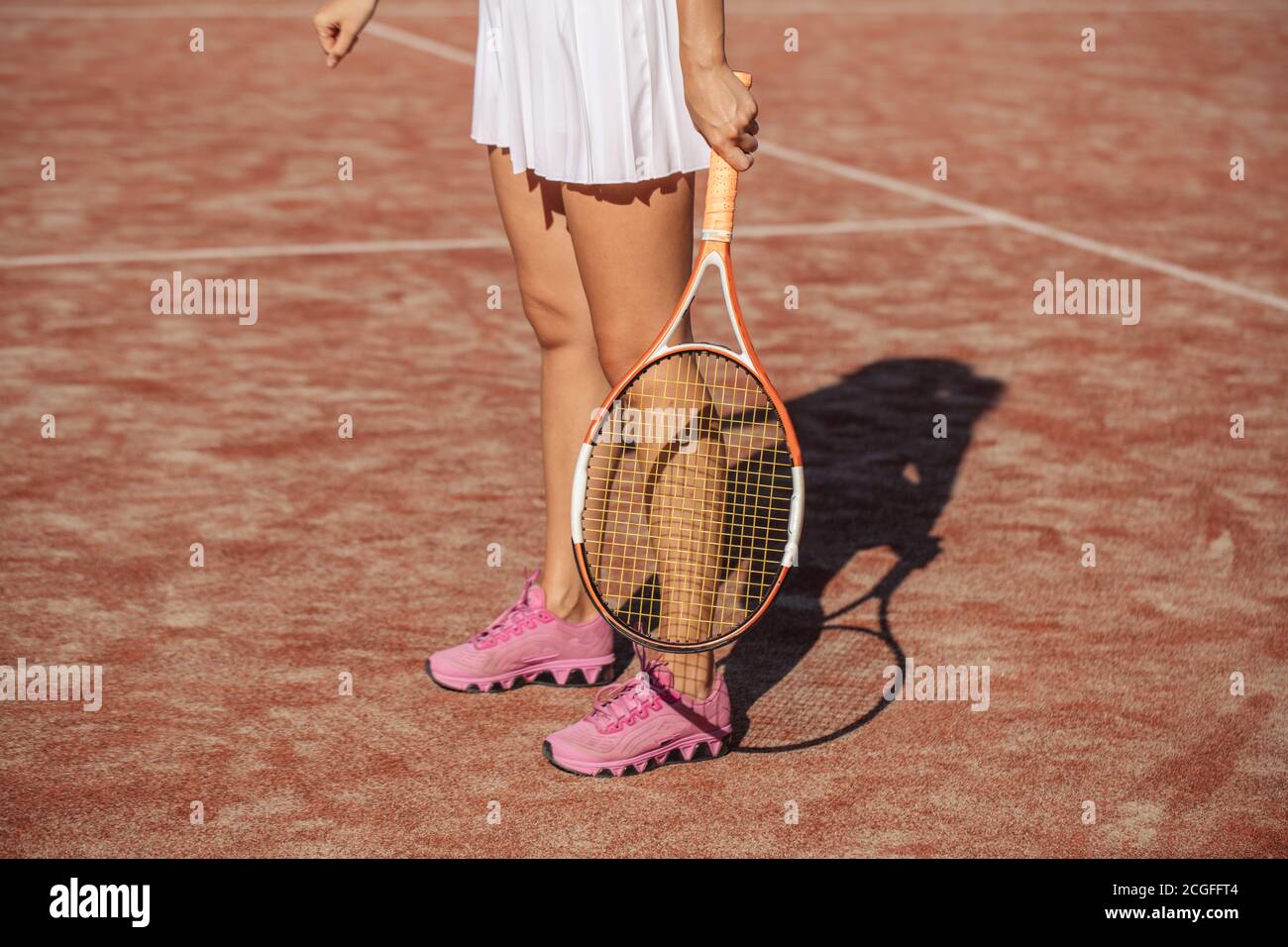 Portrait of female legs with tennis racket on red dross court, close up ...