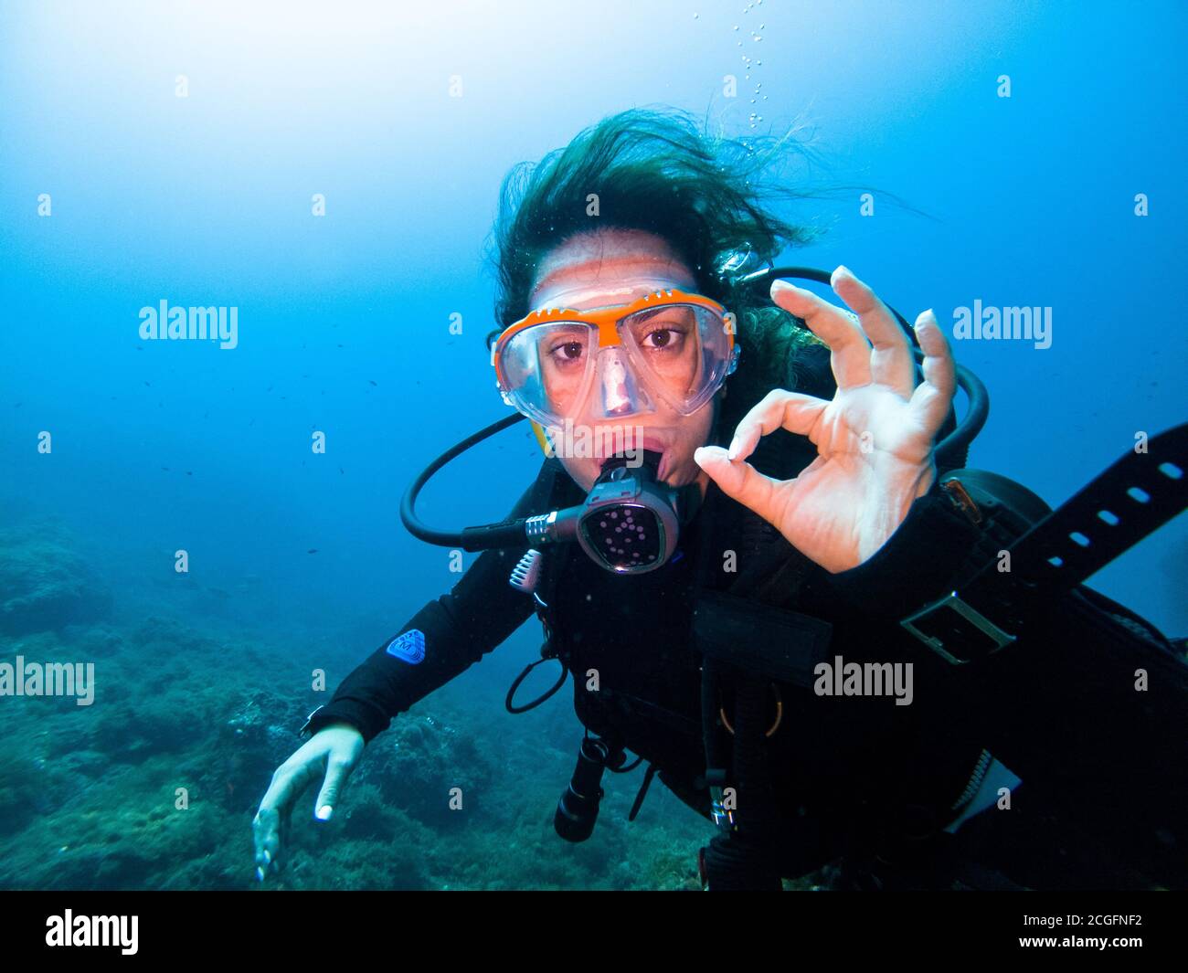A young female diver making OK sign underwater looking at the camera ...
