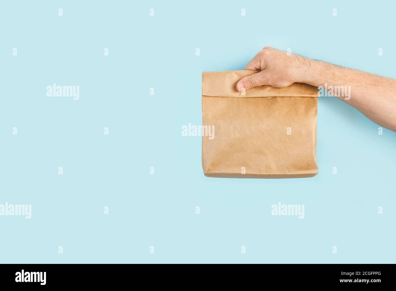 Man´s hand holding a brown paper bag on a light blue background Stock ...
