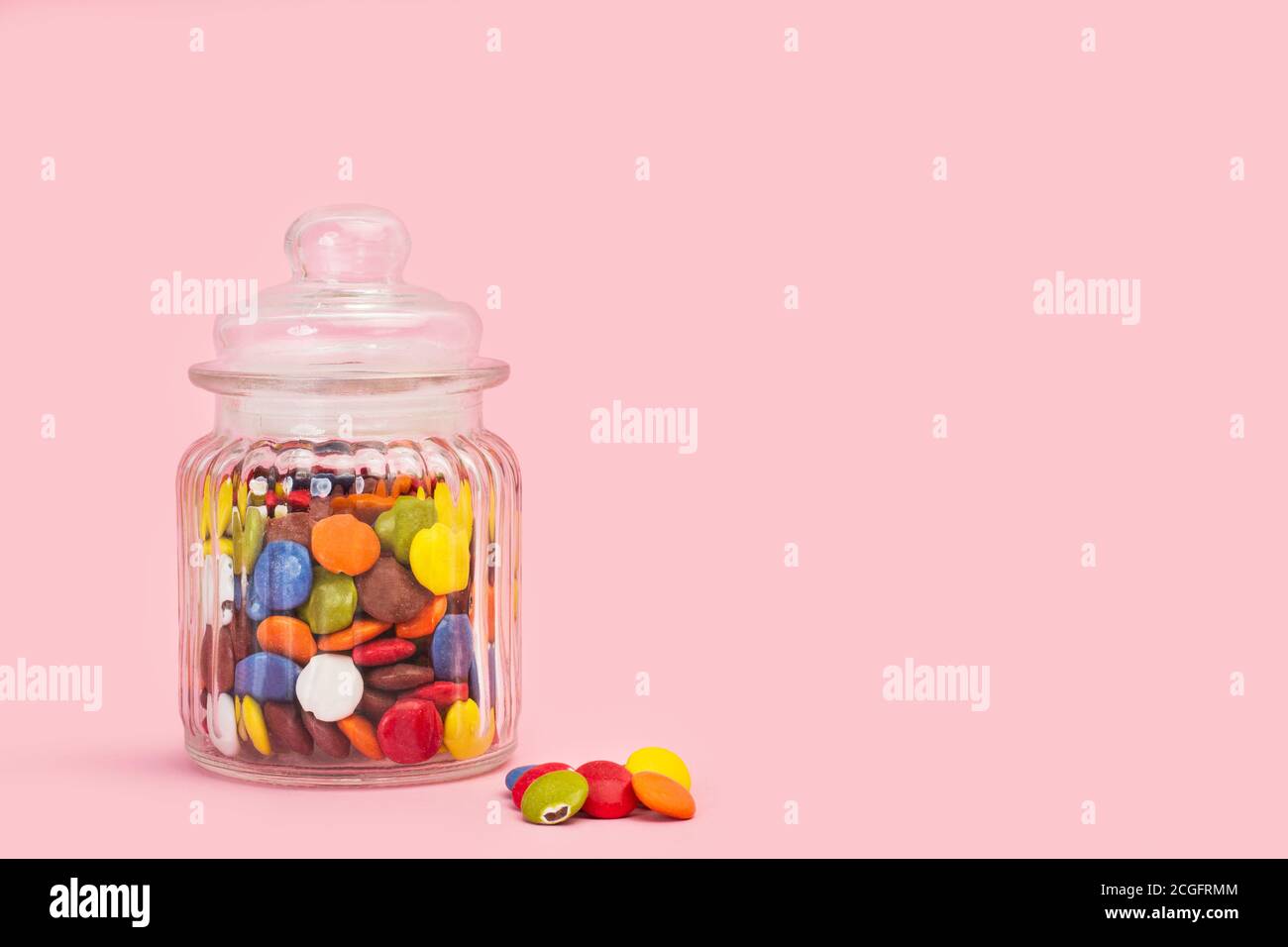 Hard shell chocolate candies in a crystal jar and on a pink background ...