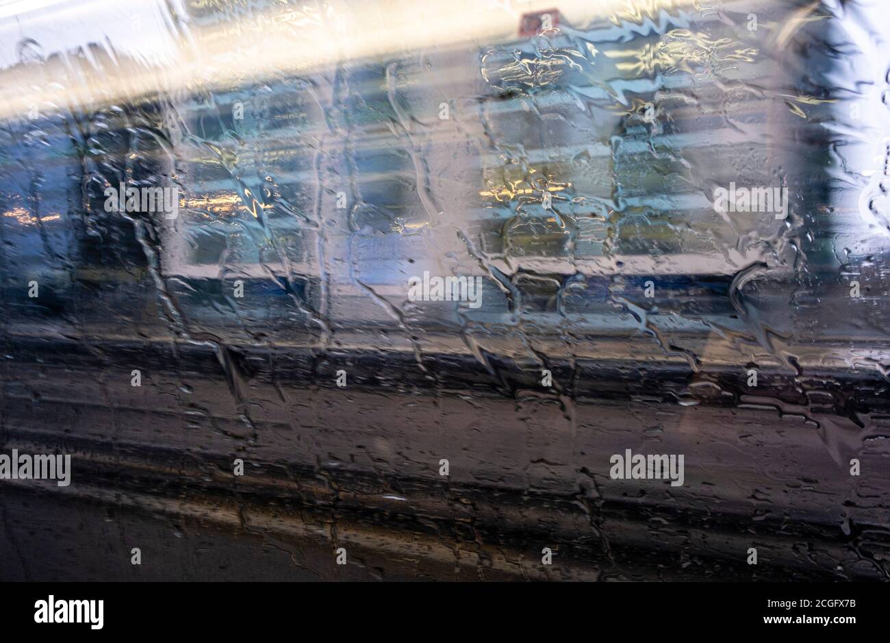 Rain on a train window obscuring the view of station, fields and ...