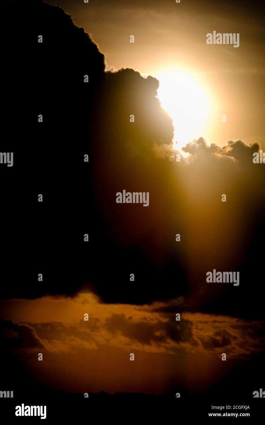 The sun appears from behind a large dark cloud throwing rays of light ...