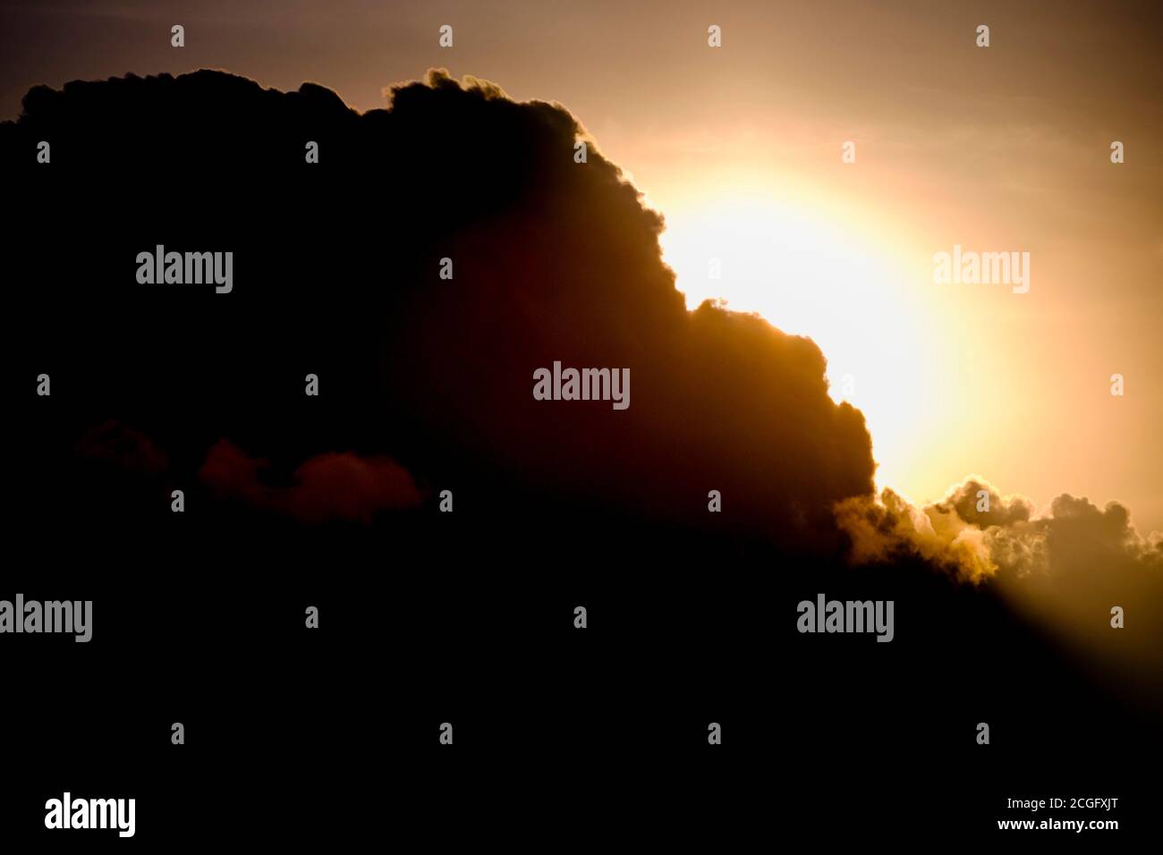 The sun appears from behind a large dark cloud throwing rays of light ...