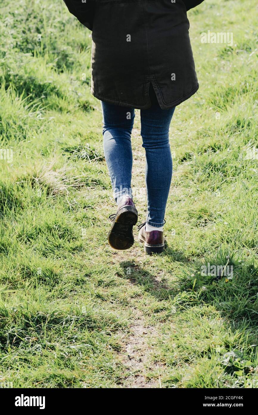 A young womans lower body and legs seen walking on a grassy country pat ...