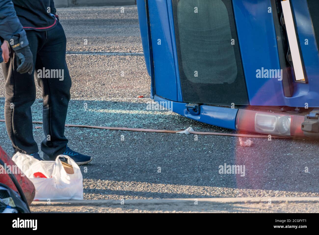 The back of an inverted blue minivan on the road and the legs of people ...