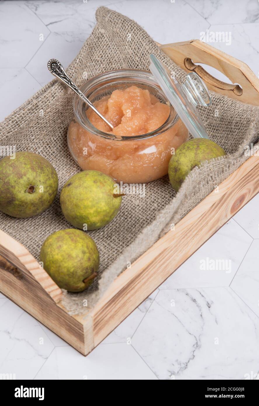 Wooden tray with a jar of mashed pears and fresh pears on a light ...
