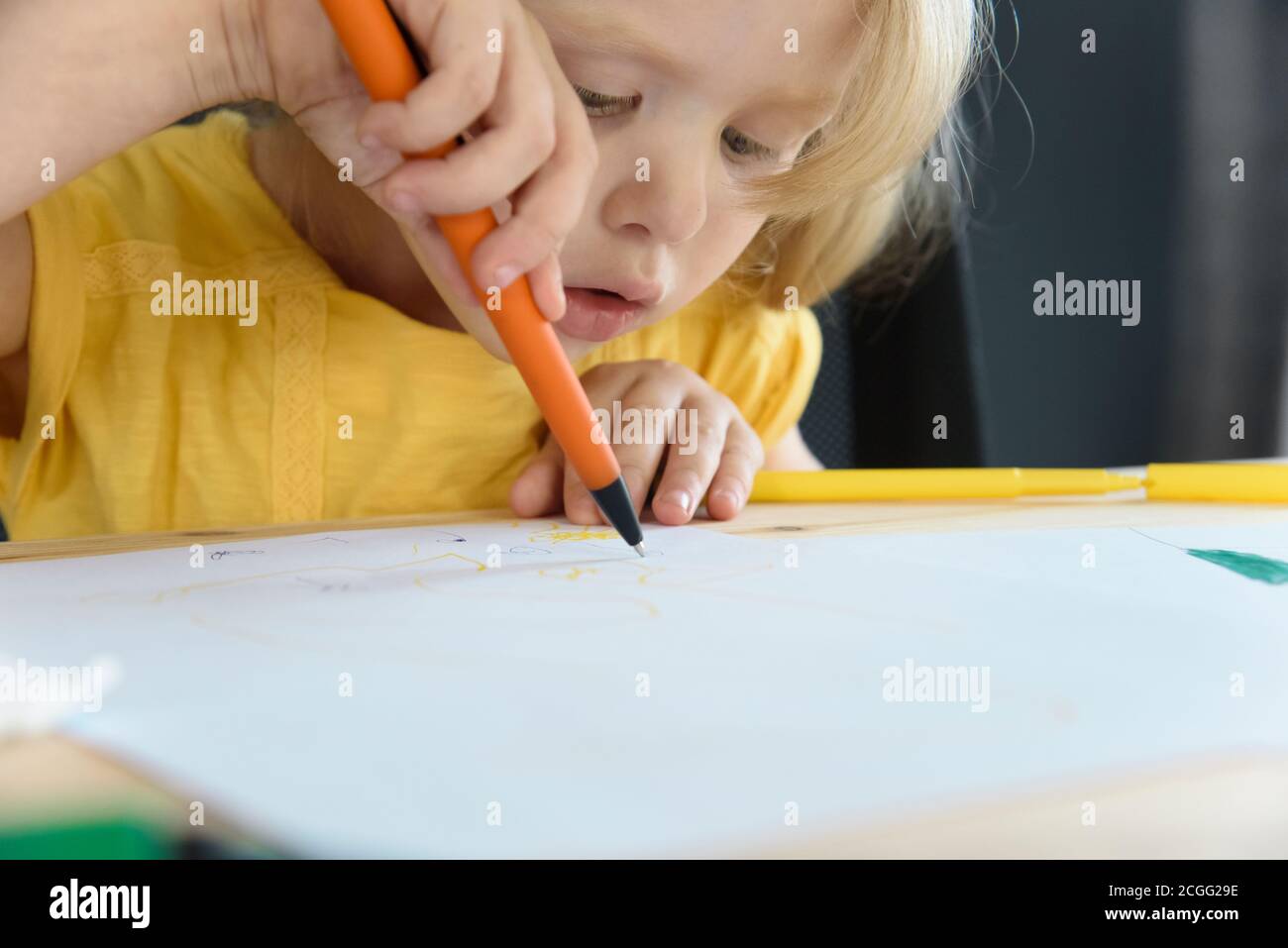 A little girl draws on a white sheet of paper. The child holds the pen ...