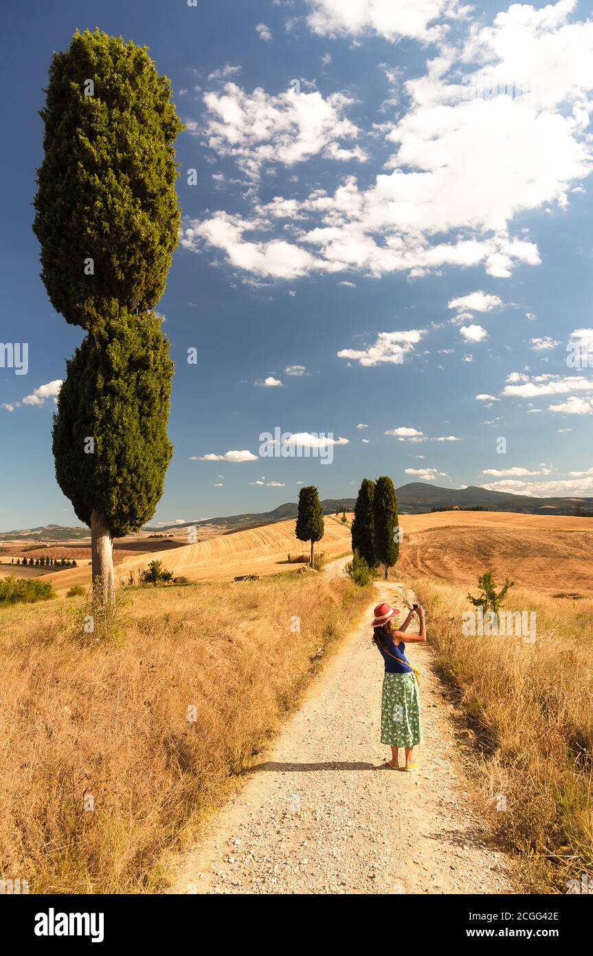 A woman stands in the middle of a country road lined with Cypress tress ...