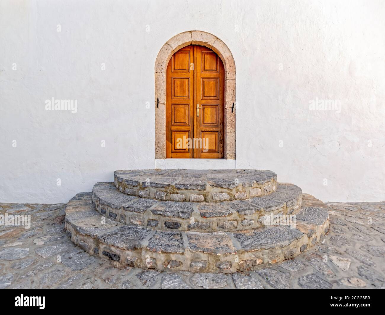 A natural wooden door with an arched stone frame on a white-washed wall ...