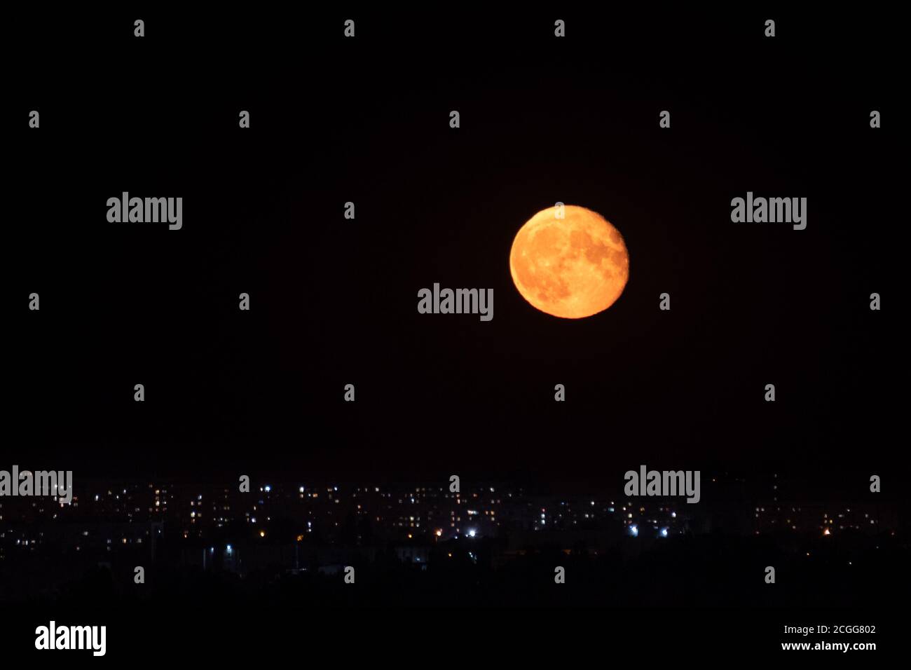 Big full red orange moon rising up on dark night sky above city lights ...