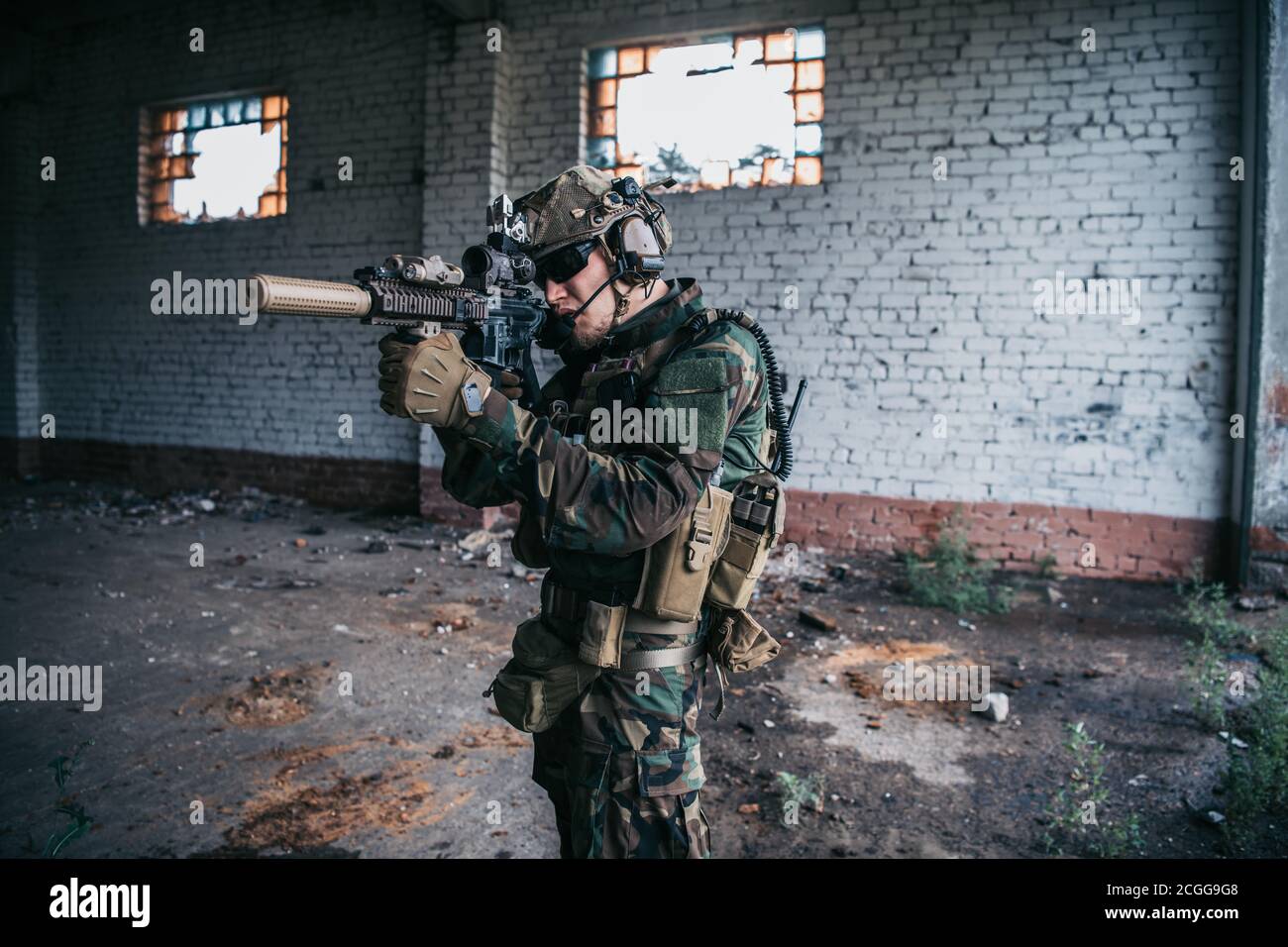 Military man with assault rifle standing inside building, he is ready ...