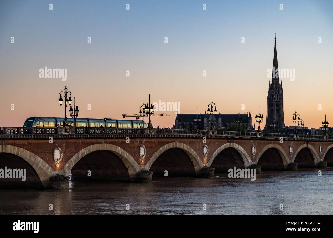 Street lights lit up at sunset, tram crossing Pont de Pierre bridge in ...