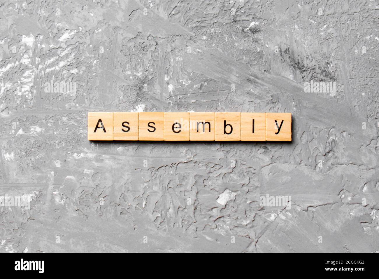 ASSEMBLY word written on wood block. ASSEMBLY text on cement table for ...