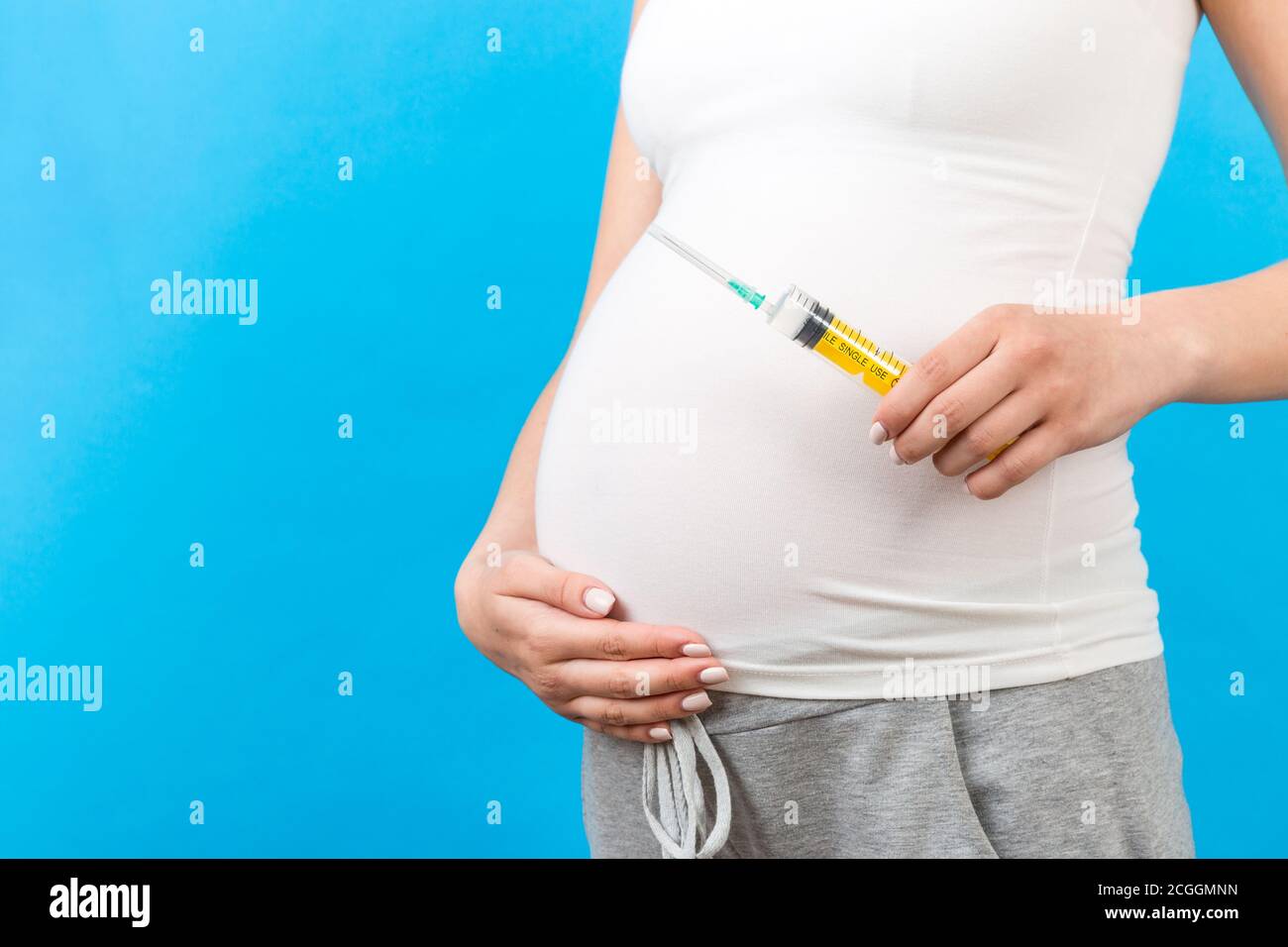 Close up of pregnant woman holding a syringe against her belly at ...