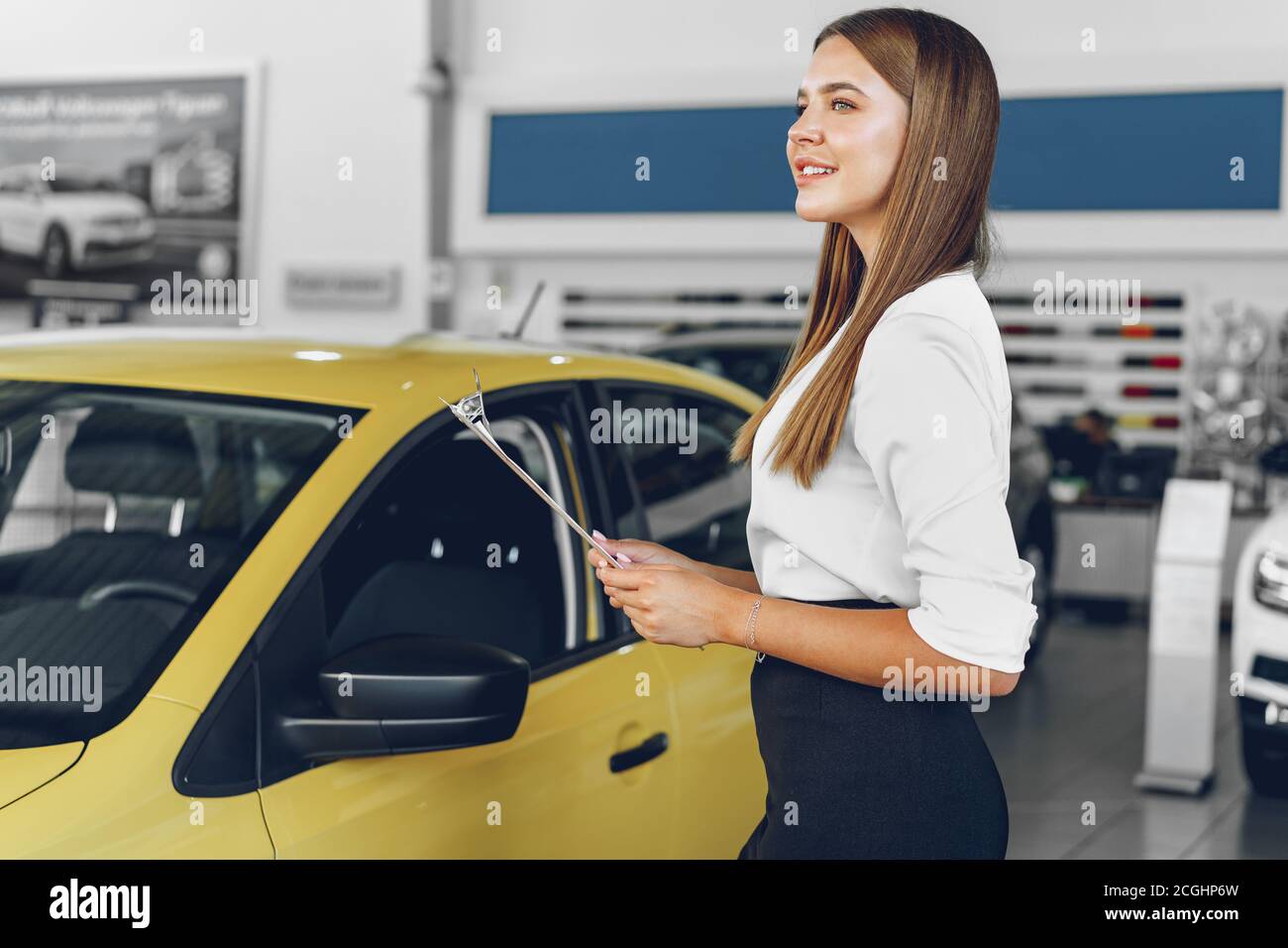 Attractive young female car dealer standing in showroom Stock Photo - Alamy