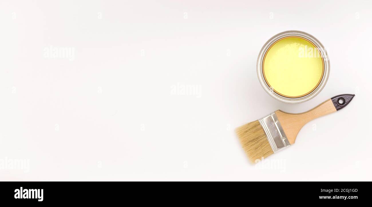 A paintbrush and a can of yellow paint on the side on a light ...