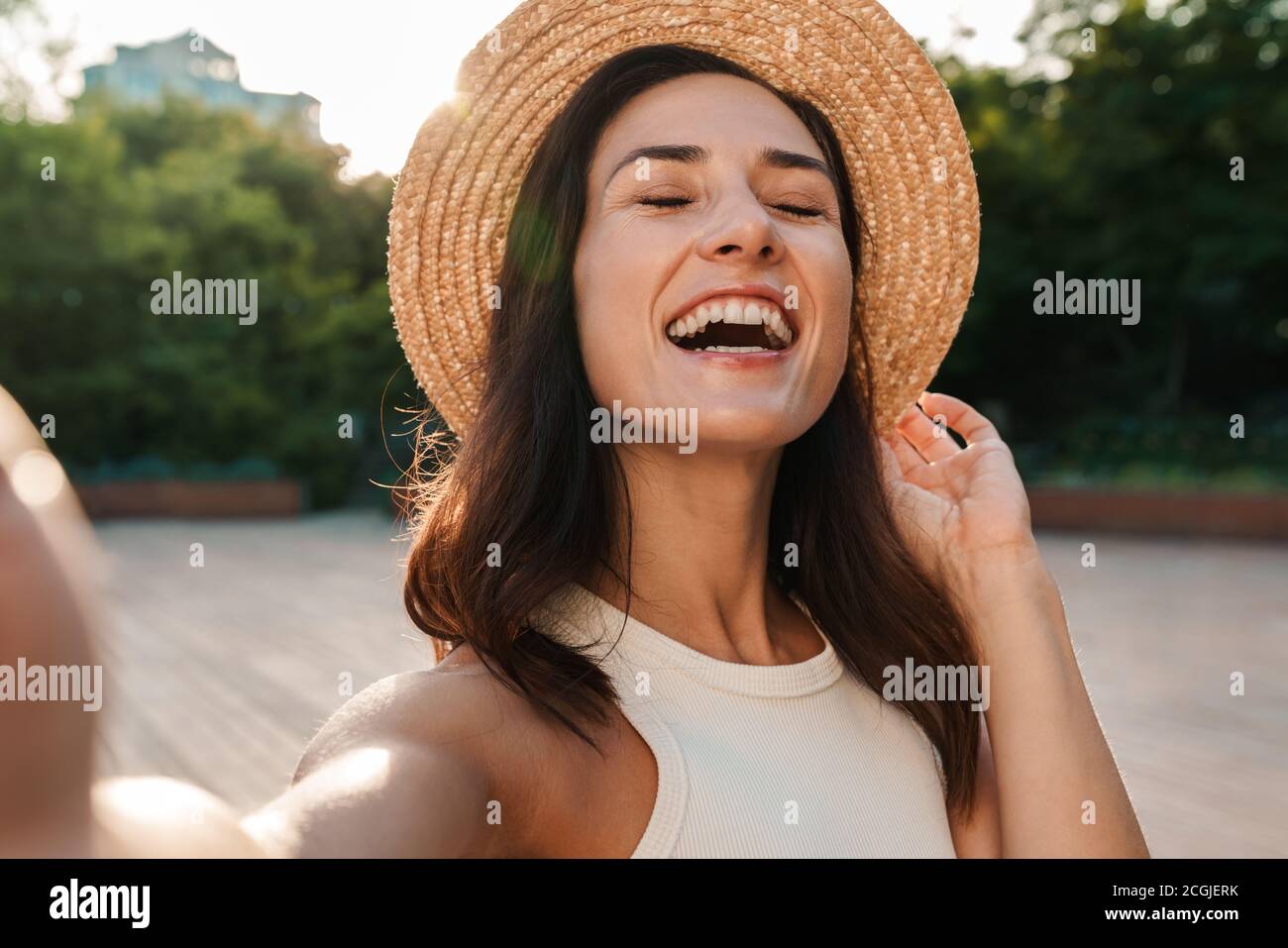Image of nice middle-aged woman wearing straw hat taking selfie photo and laughing while walking ...