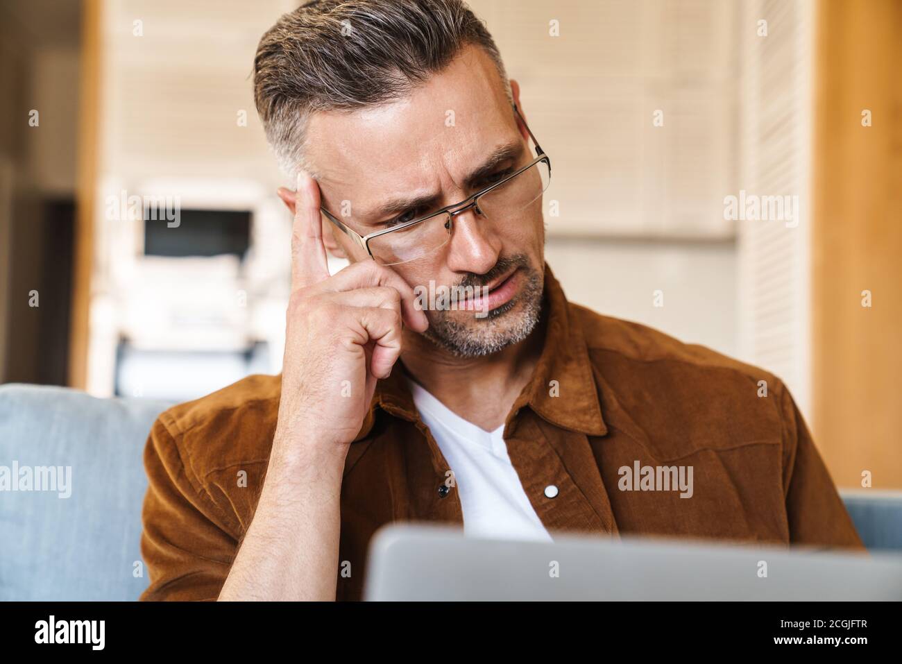 Image of perplexed adult man in eyeglasses working with laptop while ...