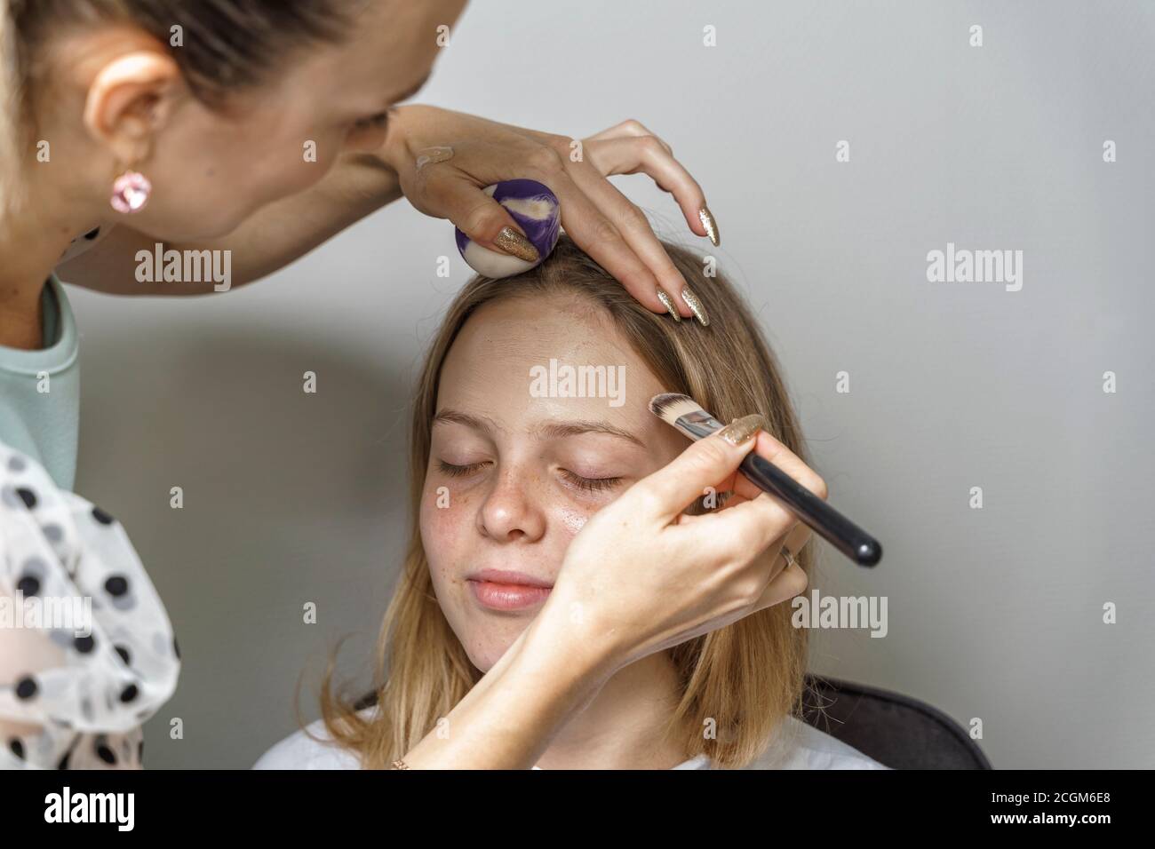 make-up artist applies a tonal foundation with a brush to the model ...