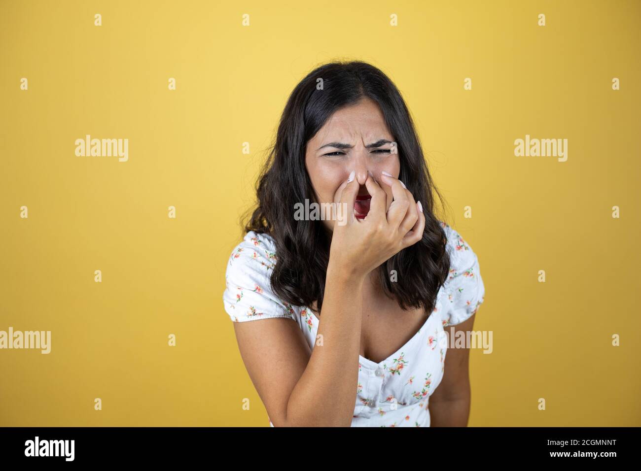 Beautiful woman over yellow background smelling something stinky and ...