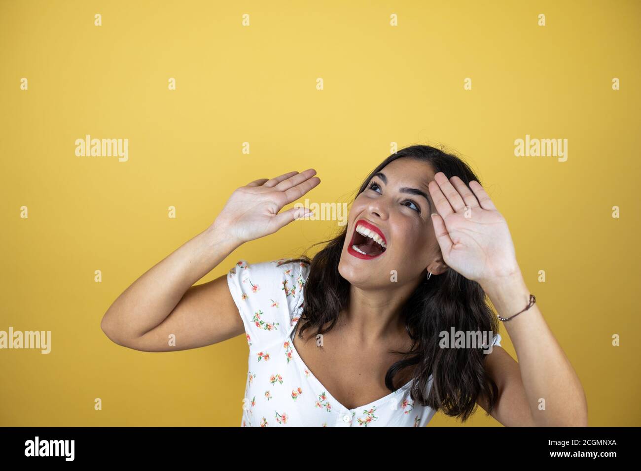 Beautiful woman over yellow background scared with her arms up like ...