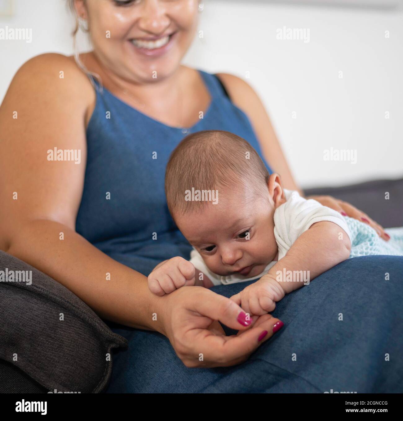 A few weeks old baby on its mother's lap, playing with her hand Stock ...