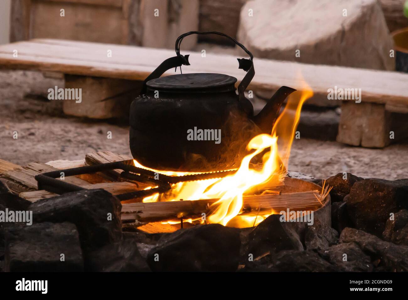 A kettle, blackened with soot, heating over a campfire surrounded with ...