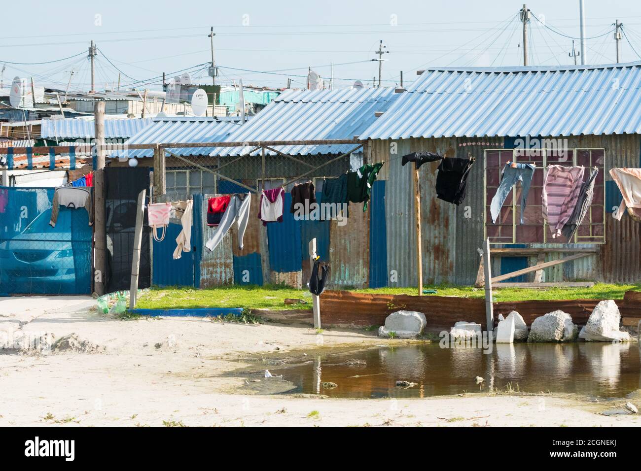tin shacks, houses and washing on a clothes line with puddles of water ...