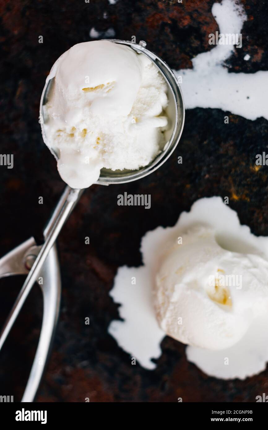 Melted ice cream in metal ice cream scooper over black rustic table ...