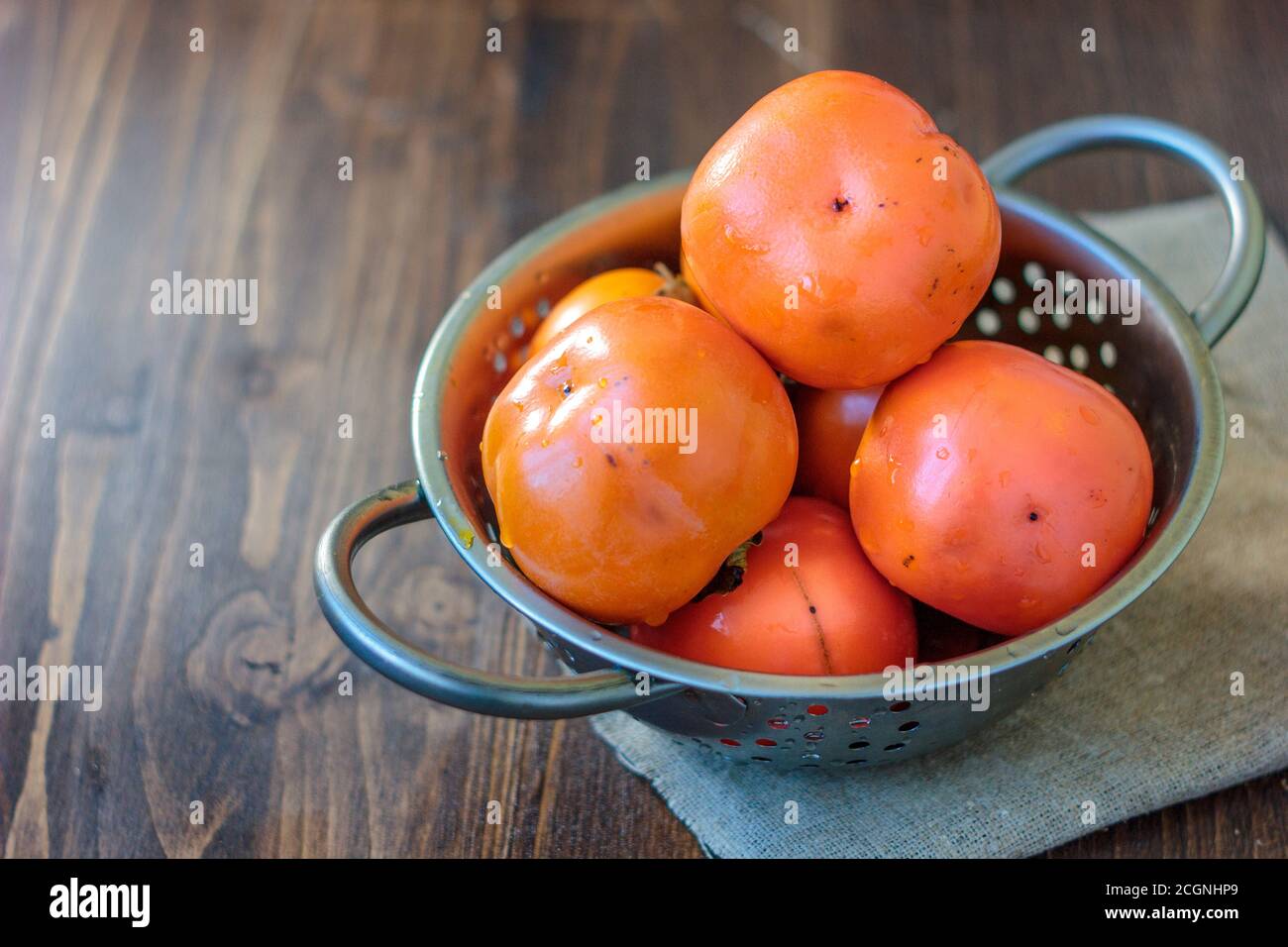 Persimmons in metal collander on wooden table Stock Photo - Alamy