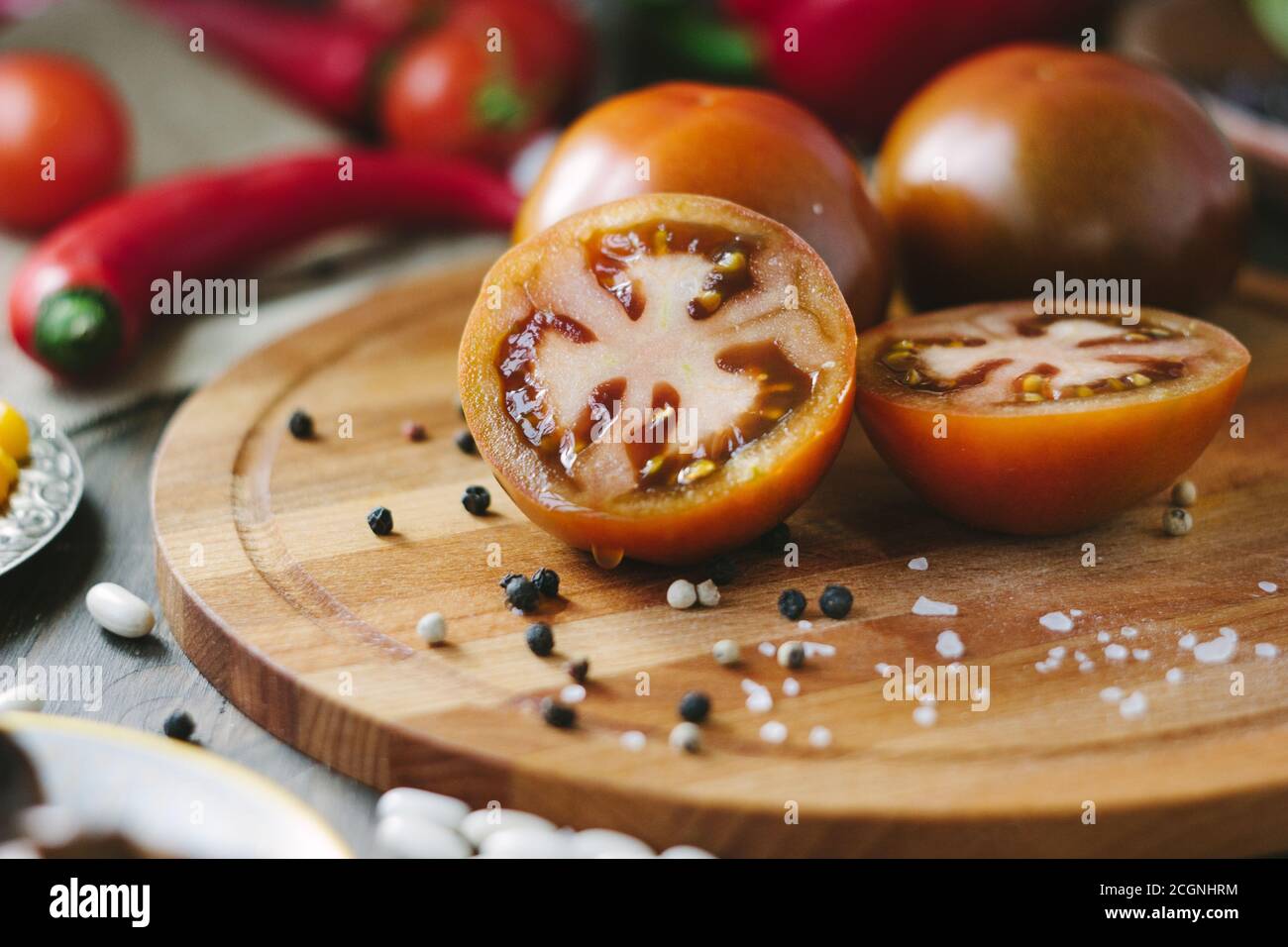 Halves of Kumato tomatoes on wooden board surrounded by vegetables and ...