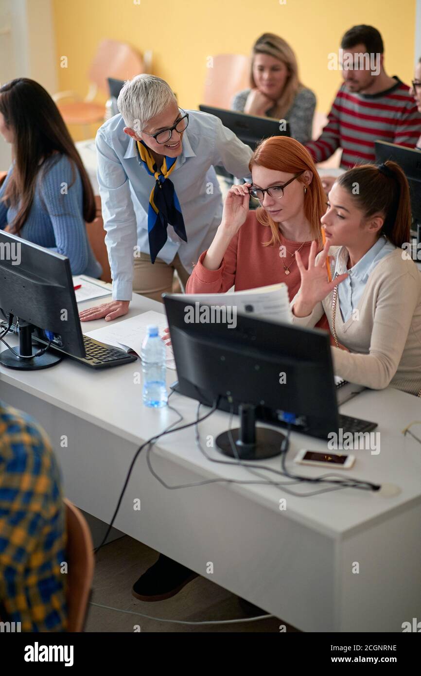 Female professor giving help to students at an informatics lecture in ...