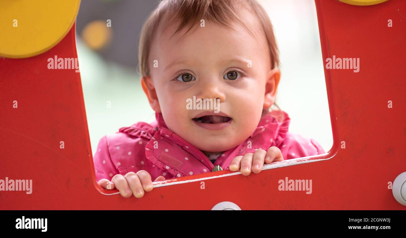 Cute baby girl having fun on a playground and looking at the camera ...