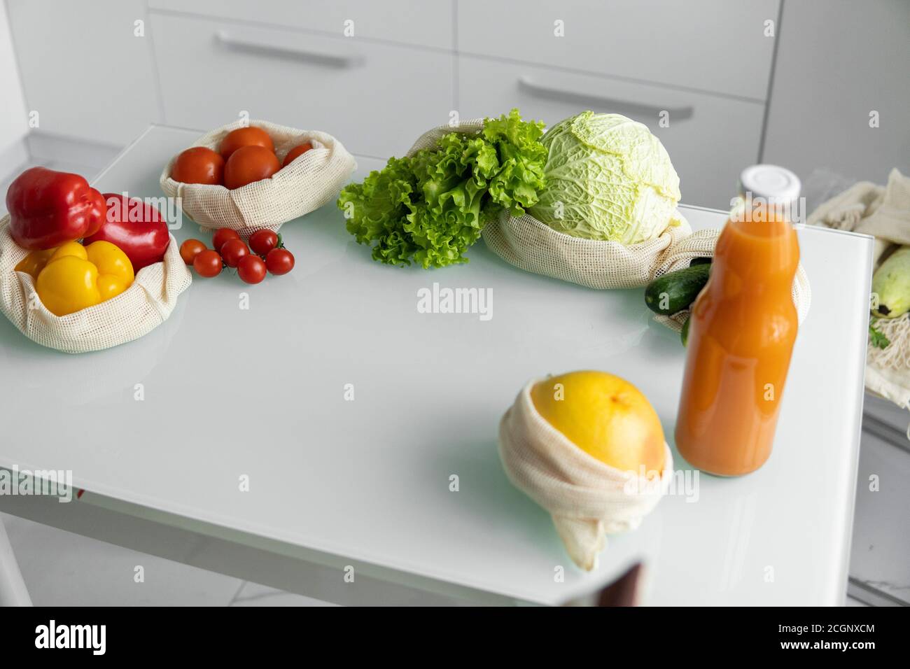 Vegetables, fruits in reusable eco cotton bags and orange juice in a ...