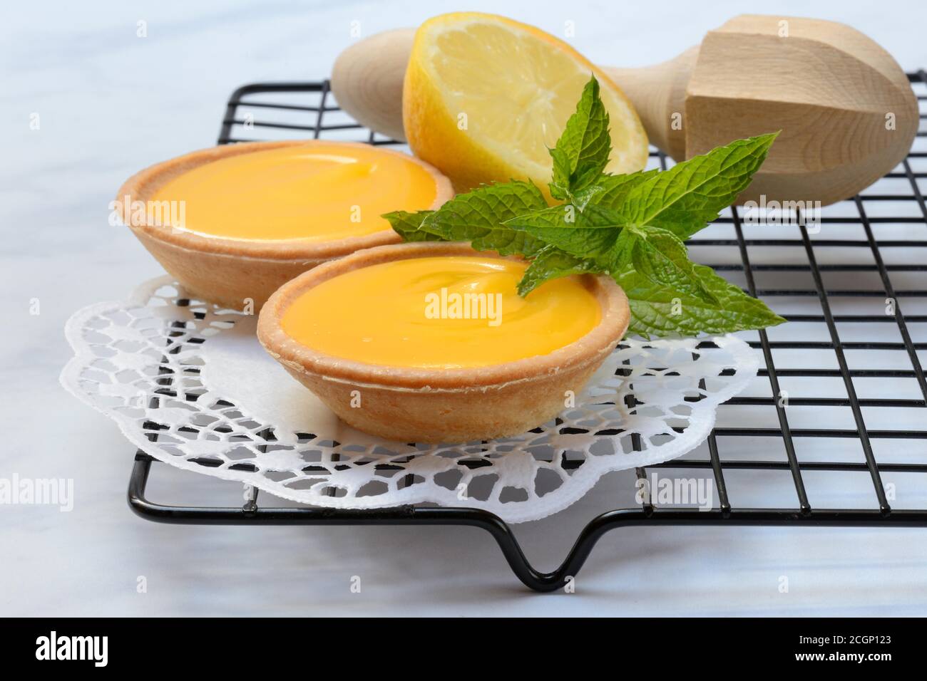 Two lemon tarts and half a lemon on a cake rack, Germany Stock Photo ...