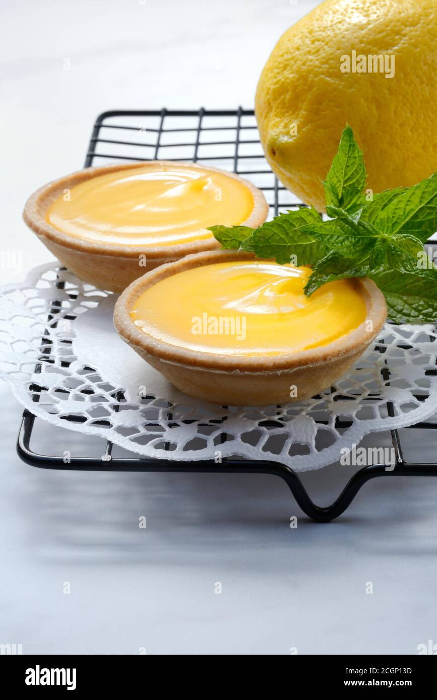 Two lemon tartlets with lemon on a cake rack hi-res stock photography ...