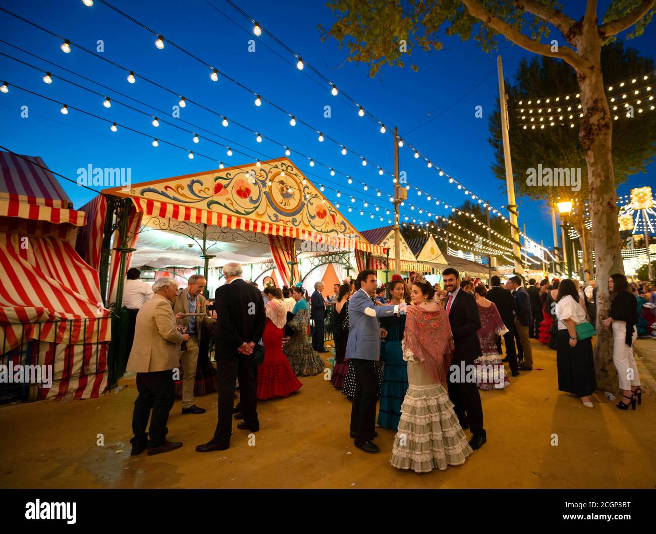 Spaniards celebrating in traditional clothes in front of lit marquees ...