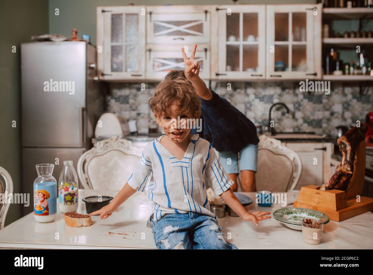 Beautiful little caucasian boy sitting on the table in the kitchen ...