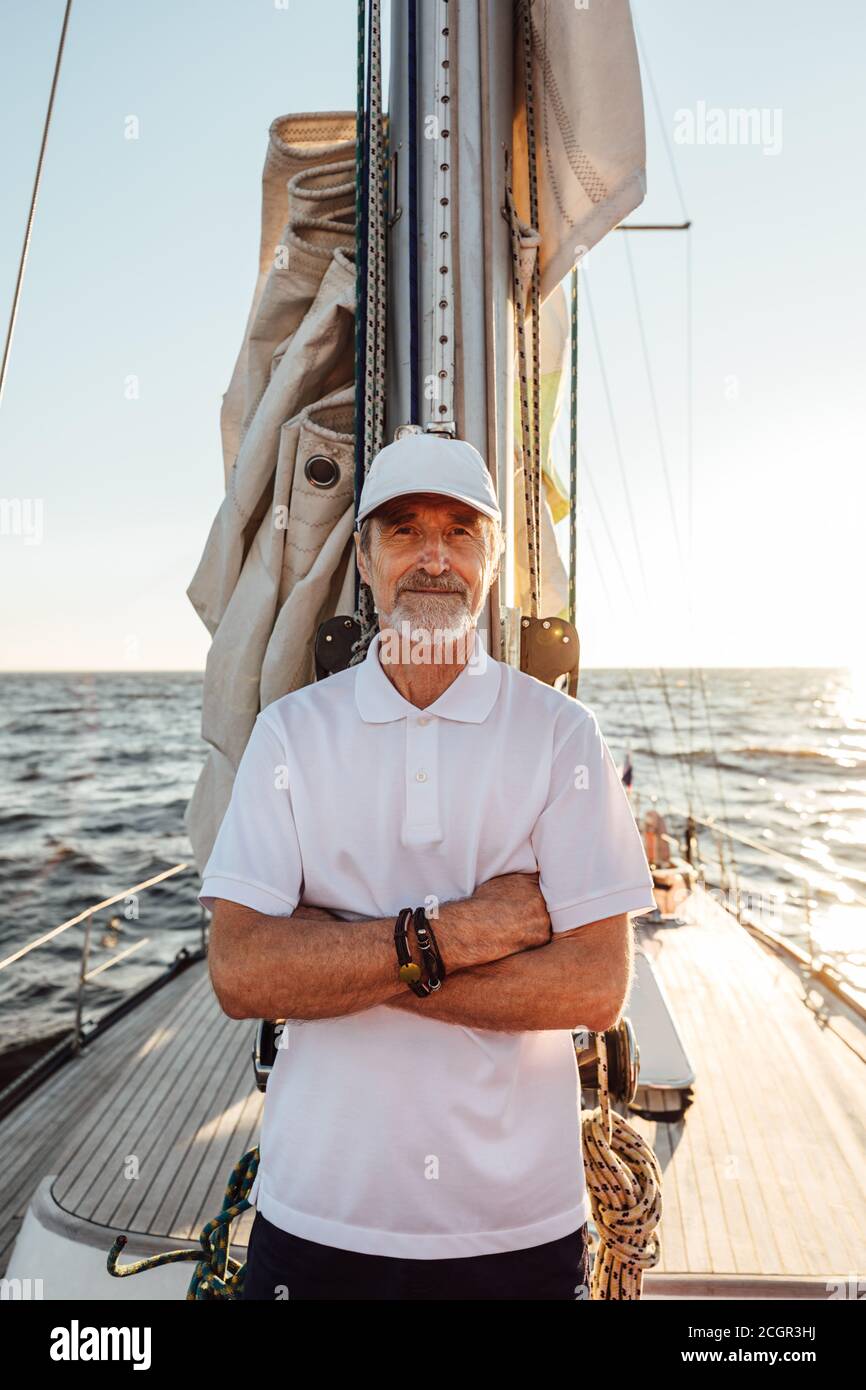 Portrait of a mature captain standing on his yacht at mast with crossed ...