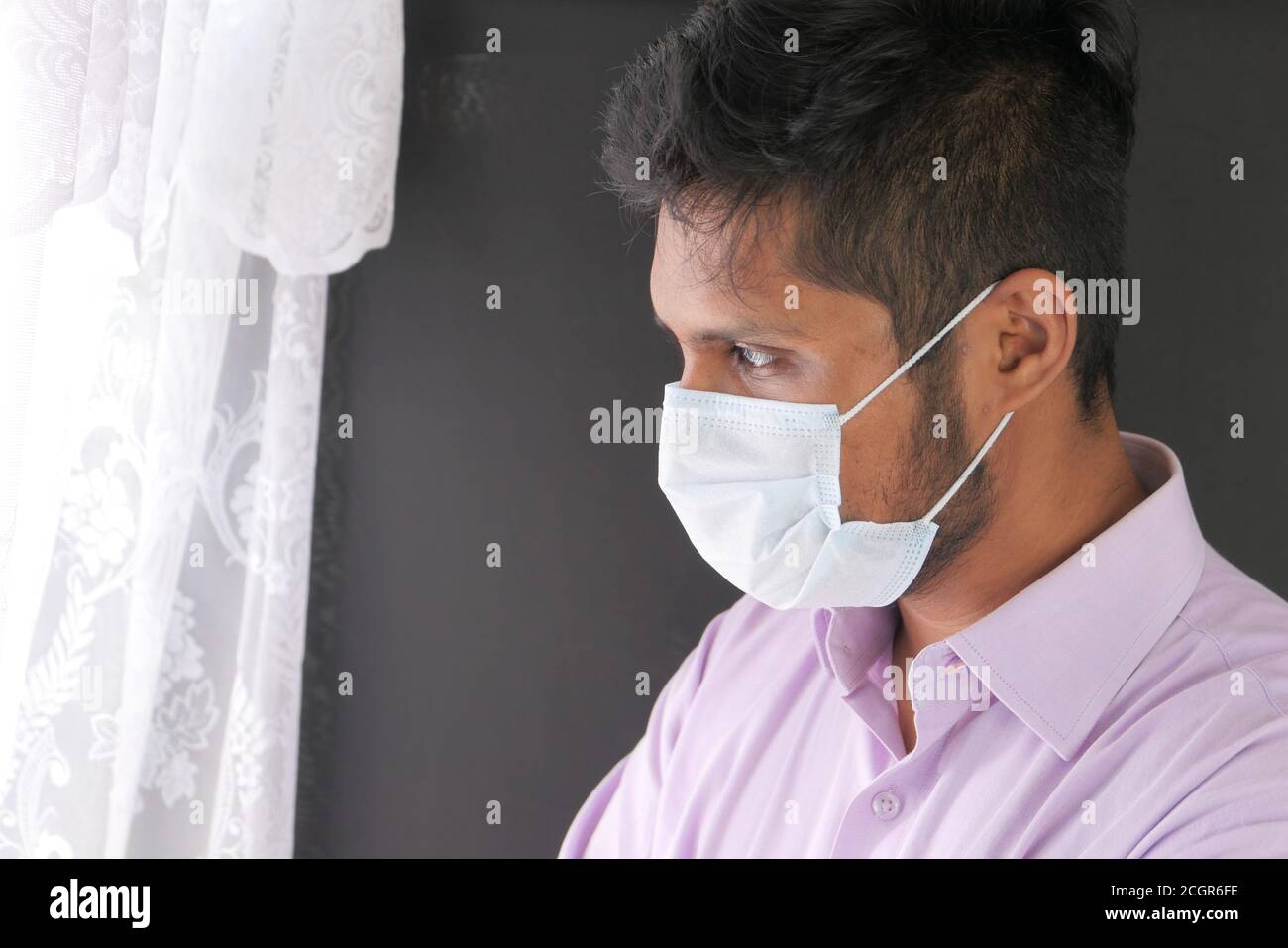 A young asian man with protective mask in face looking through window ...