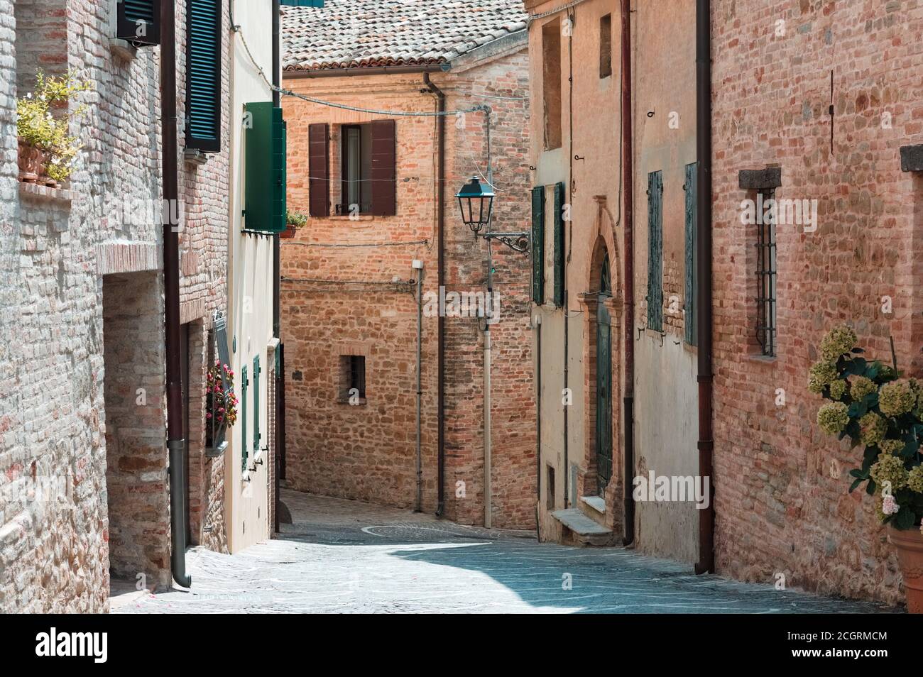Alley of an Italian village with old brick houses, plants and flowers ...