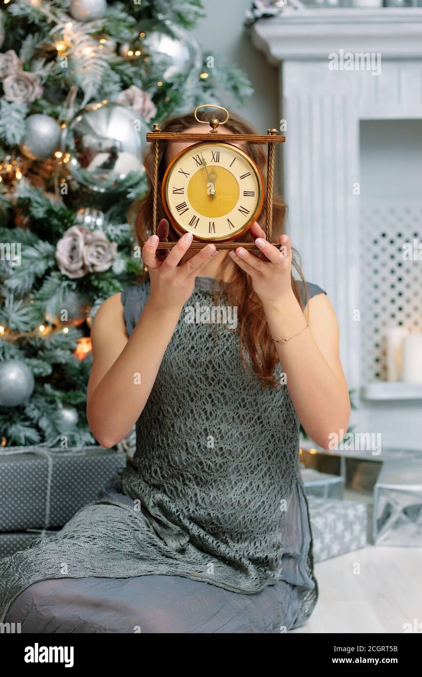 Young lady holding clocks behind face near christmas tree - christmas and new year concept Stock ...