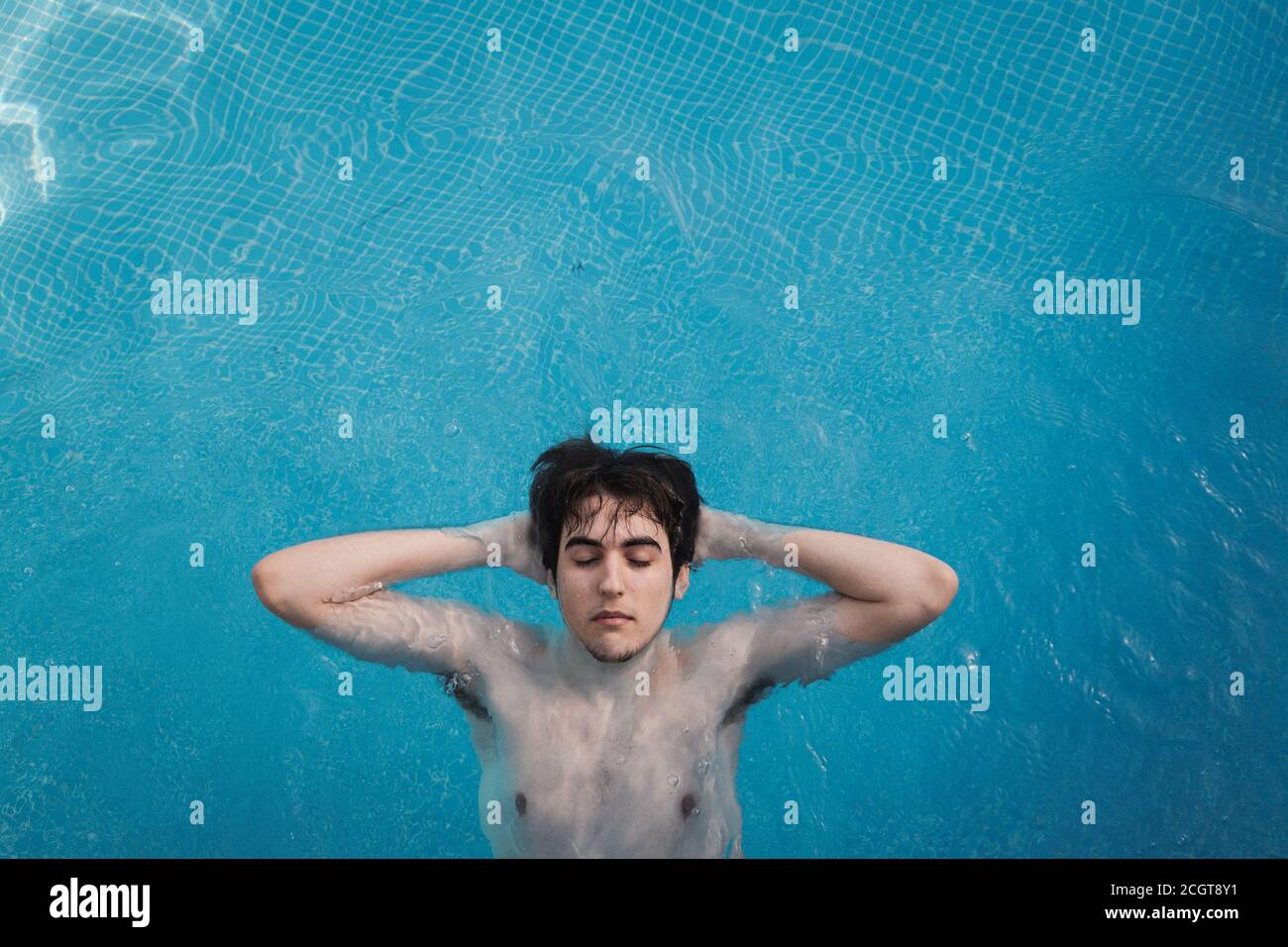 Top view of a young man with his eyes closed, floating in a swimming ...