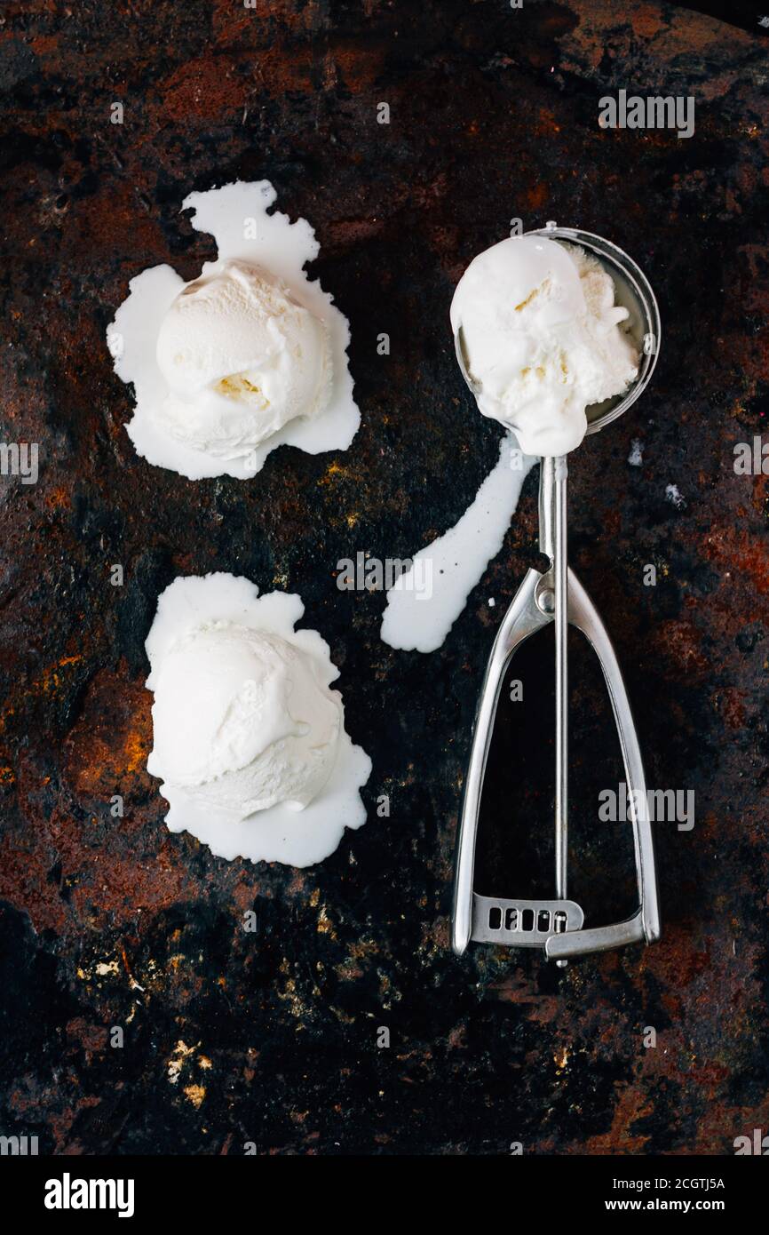 Melted ice cream in metal ice cream scooper over black rustic table ...