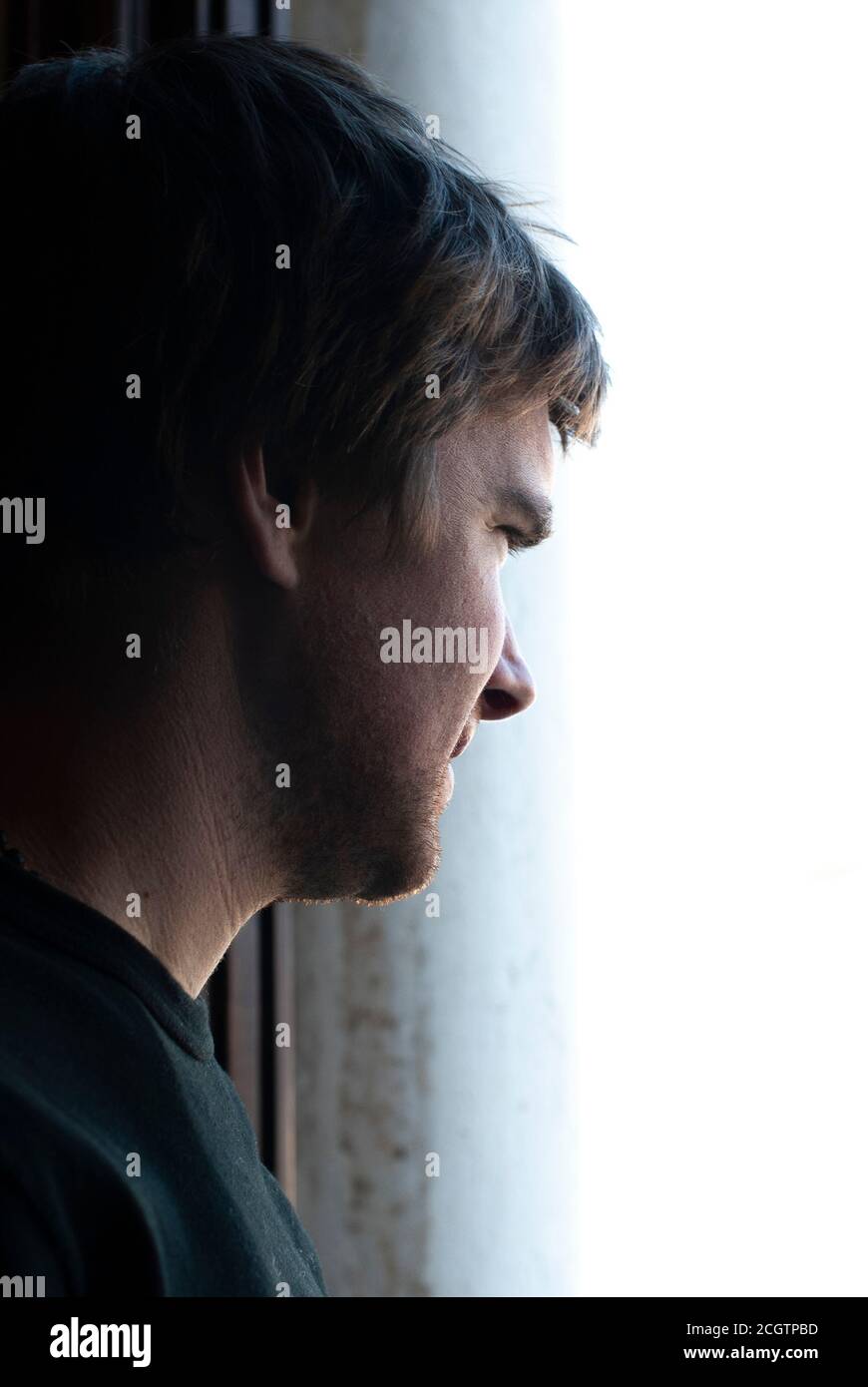 Portrait of young man looking out of window with a serious and ...