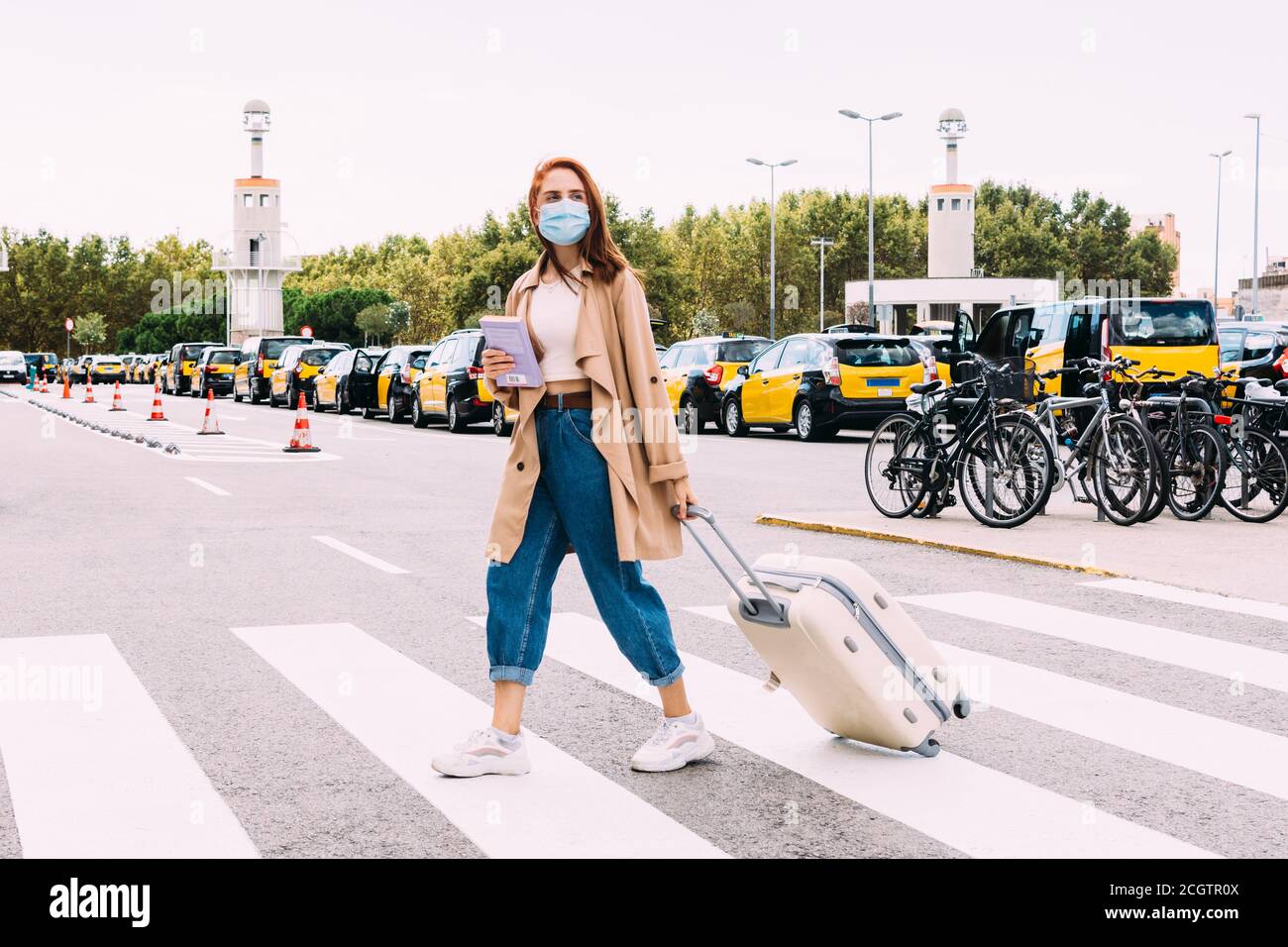 young woman with a face mask crosses the street to take a cab out of ...
