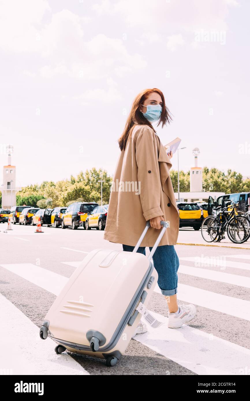 young woman with a face mask crosses the street to take a cab out of ...
