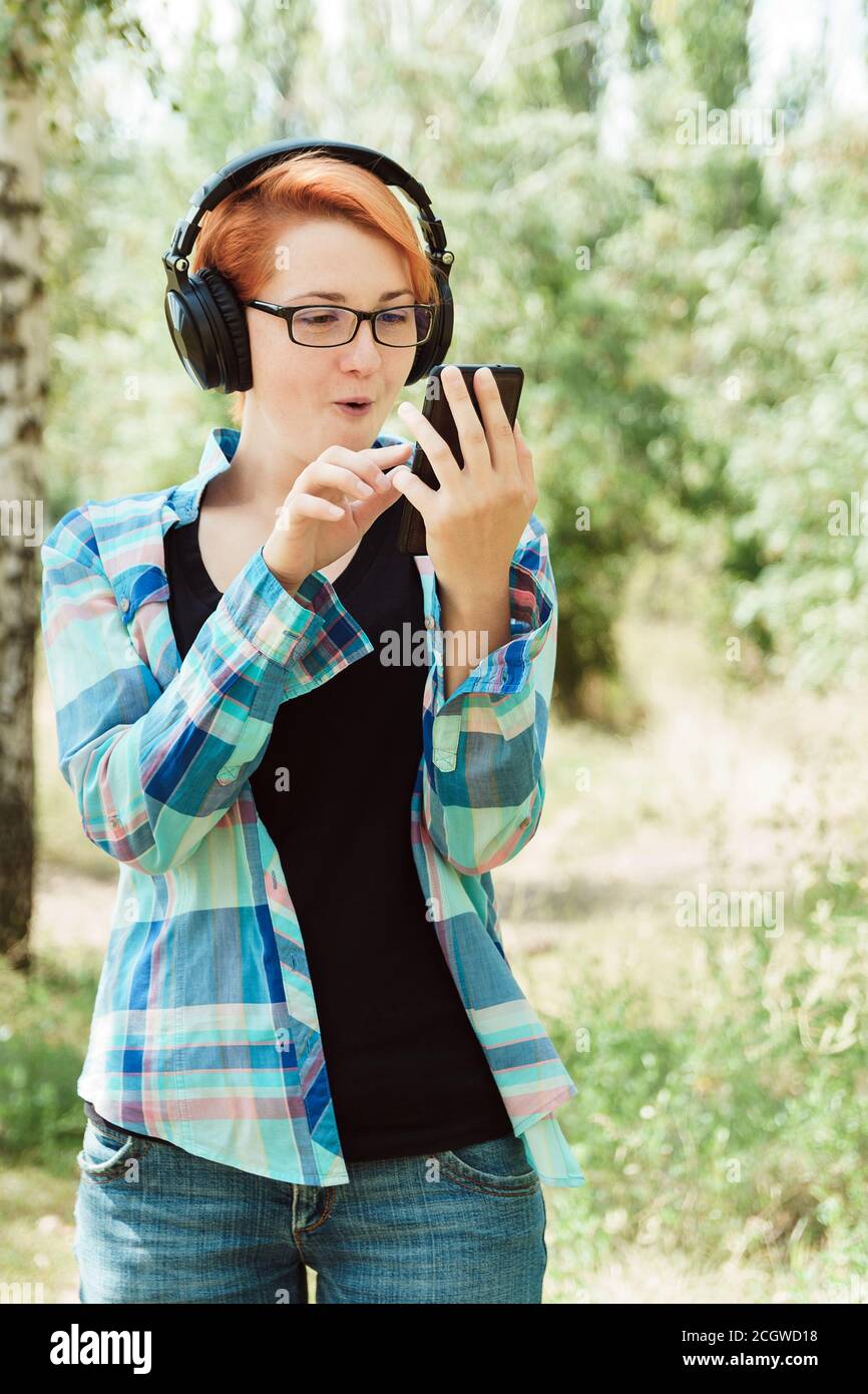 Cute ginger girl looking at smartphone. Beautiful woman in summer park ...