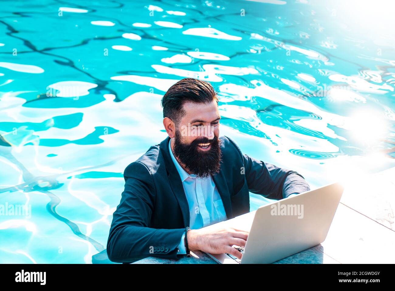 Happy businessman in suit with laptop in swimming pool. Funny business ...